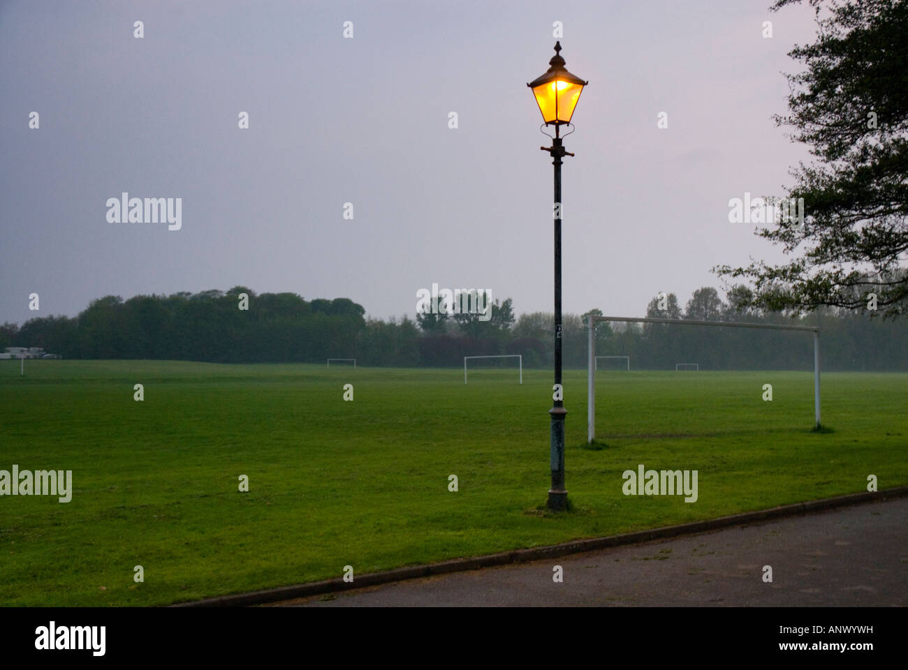 Park and football field at dusk with lighted lampost in foreground ...