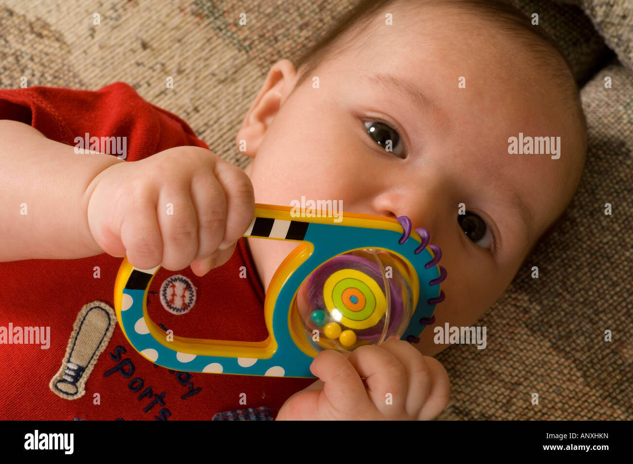 3 month old baby boy closeup on back holding and biting mouthing toy ...