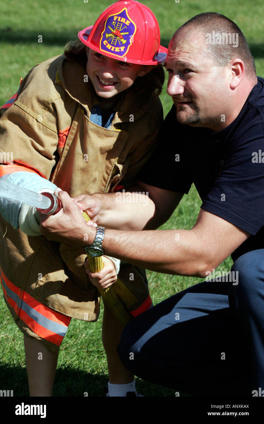 A firefighter helping a future firefighter young child to use a hose at ...