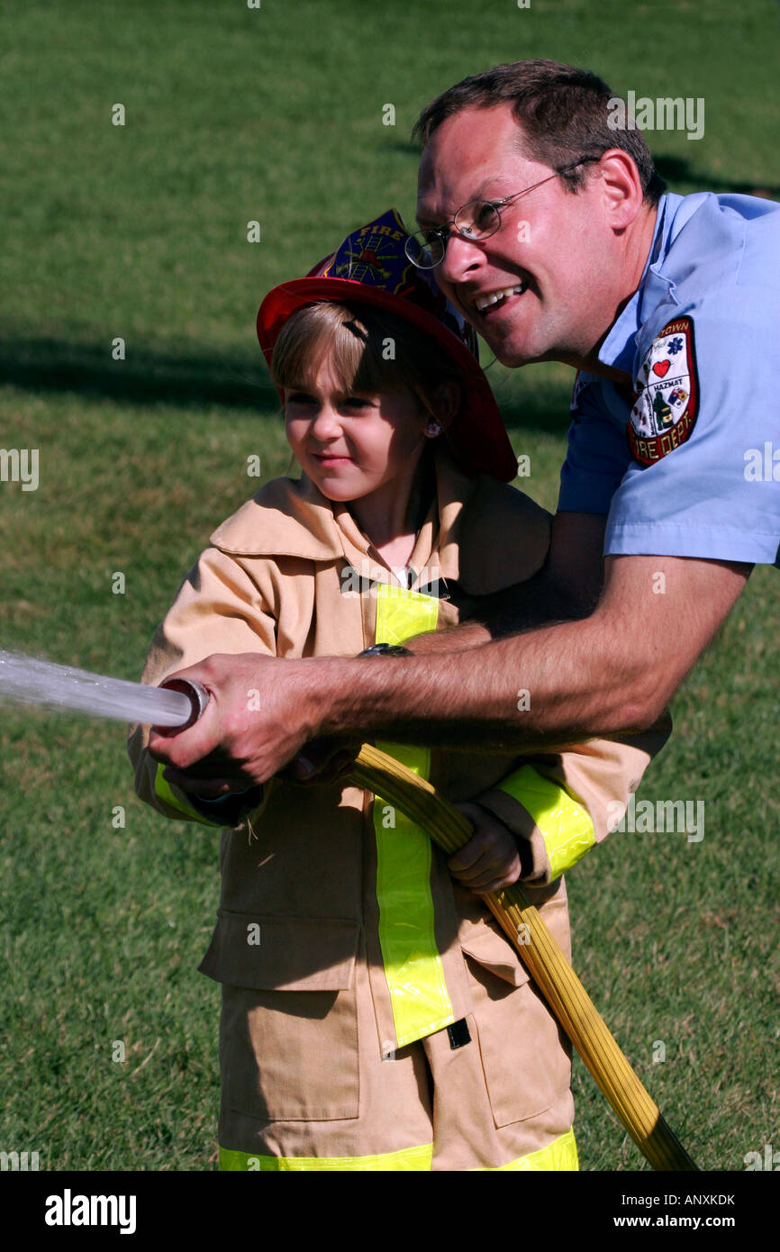 A firefighter helping a future firefighter young child to use a hose at ...
