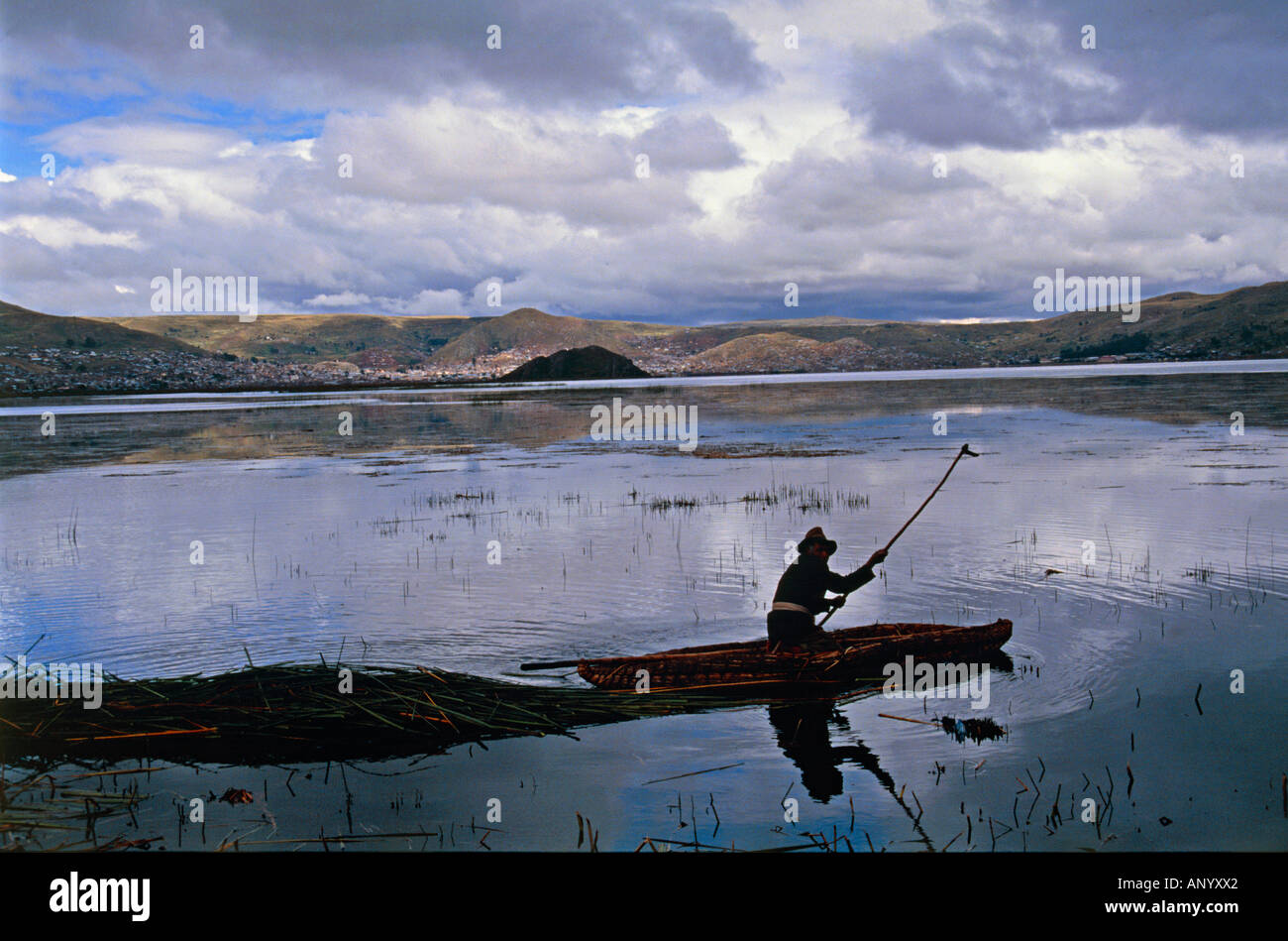 man of uros tribe riding totora reed boat at evening lake titicaca ...