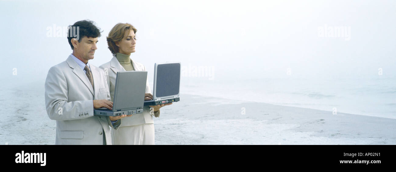 Businessman and woman standing, holding laptops on beach Stock Photo ...