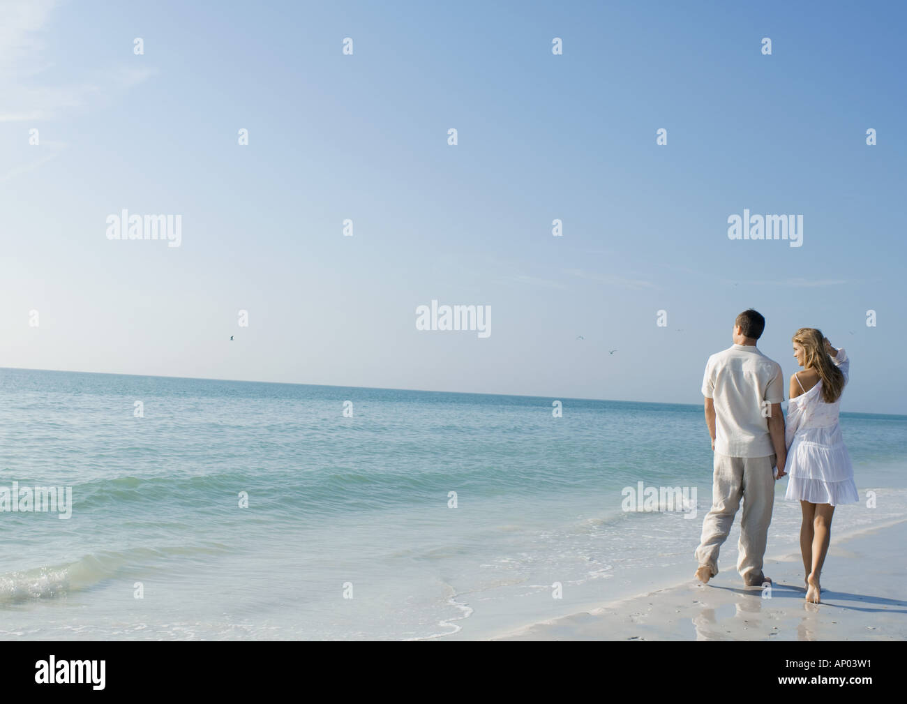 Couple walking alongside water on beach Stock Photo - Alamy