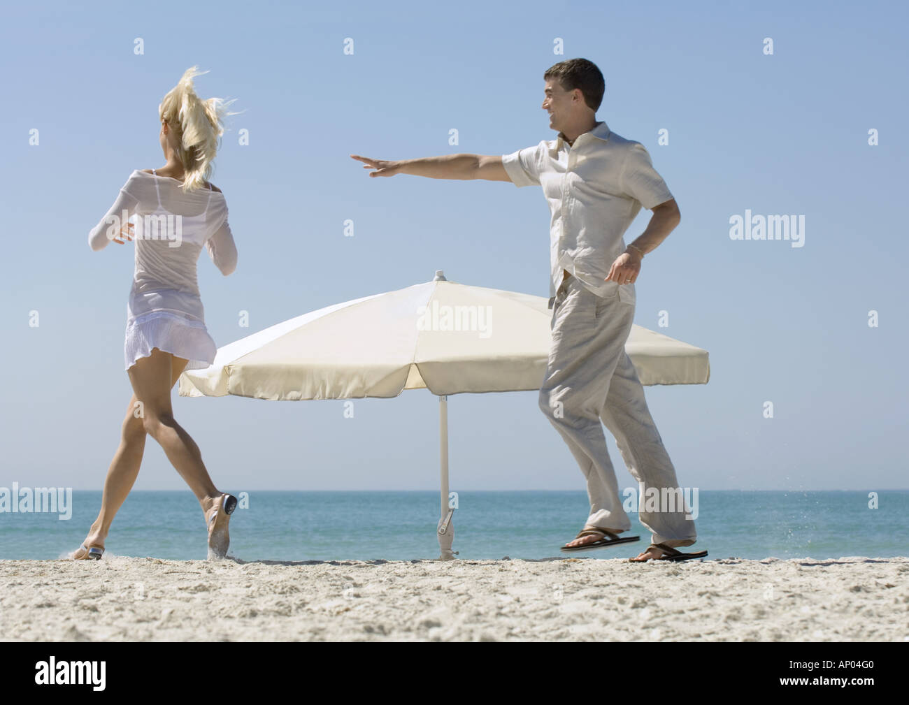 Couple chasing each other around parasol on beach Stock Photo - Alamy