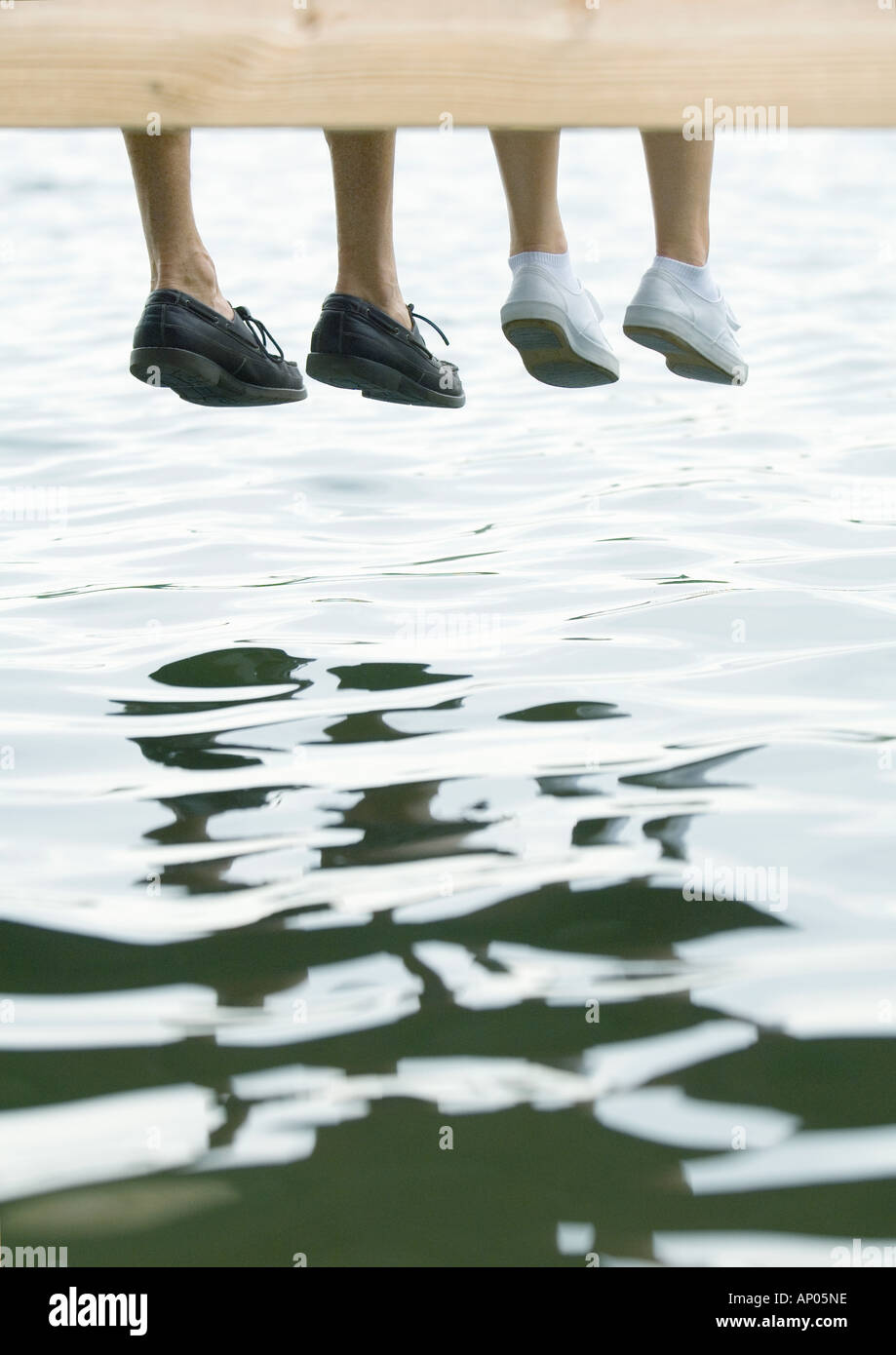 Two people sitting on dock, view of feet Stock Photo - Alamy
