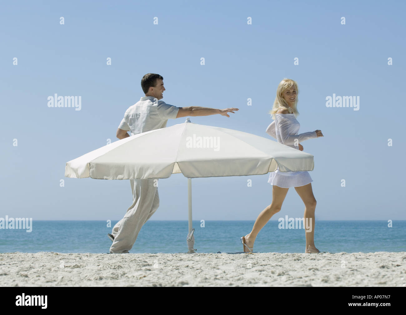 Man chasing woman around parasol on beach Stock Photo - Alamy