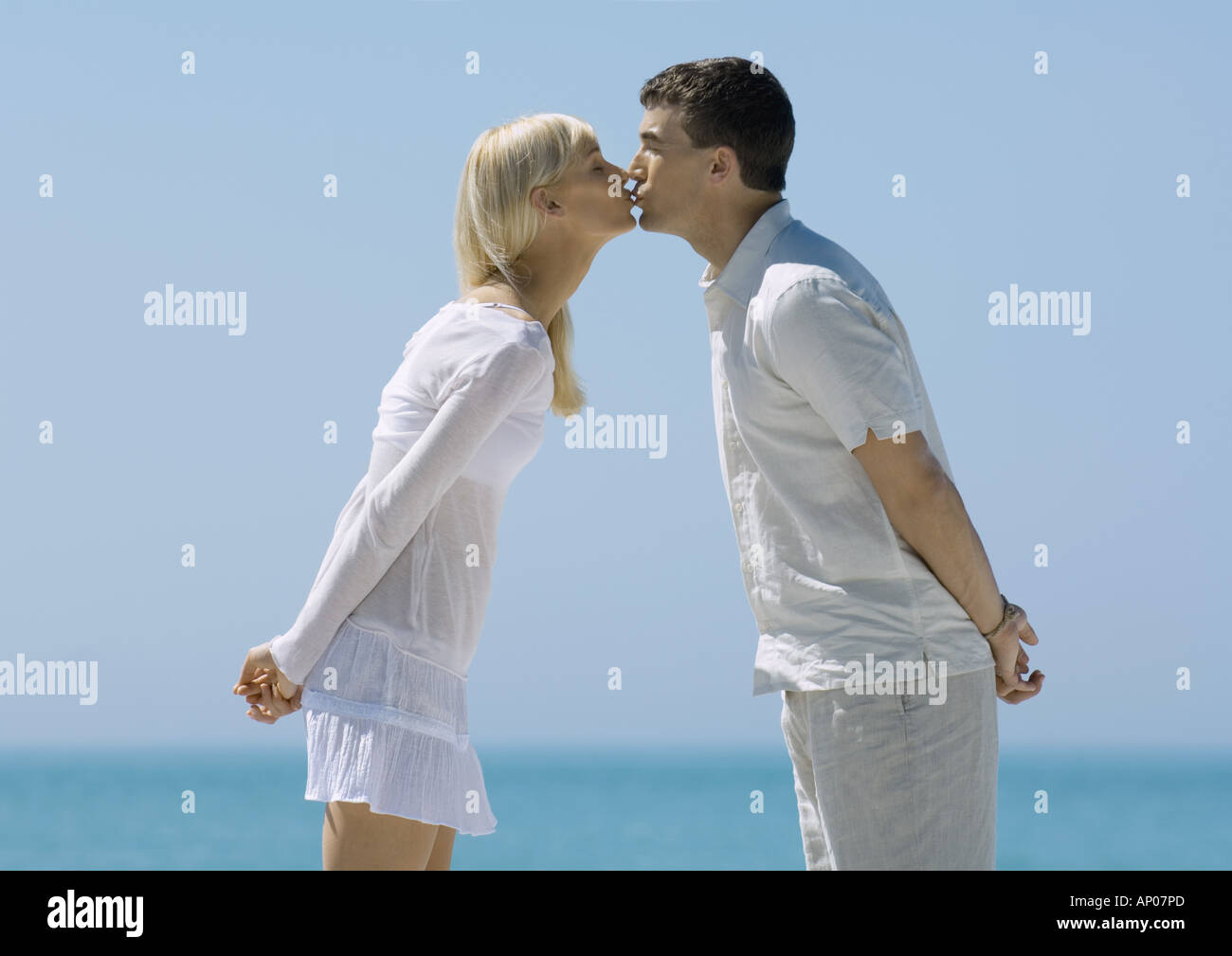 Couple leaning forward, kissing, sea in background Stock Photo - Alamy
