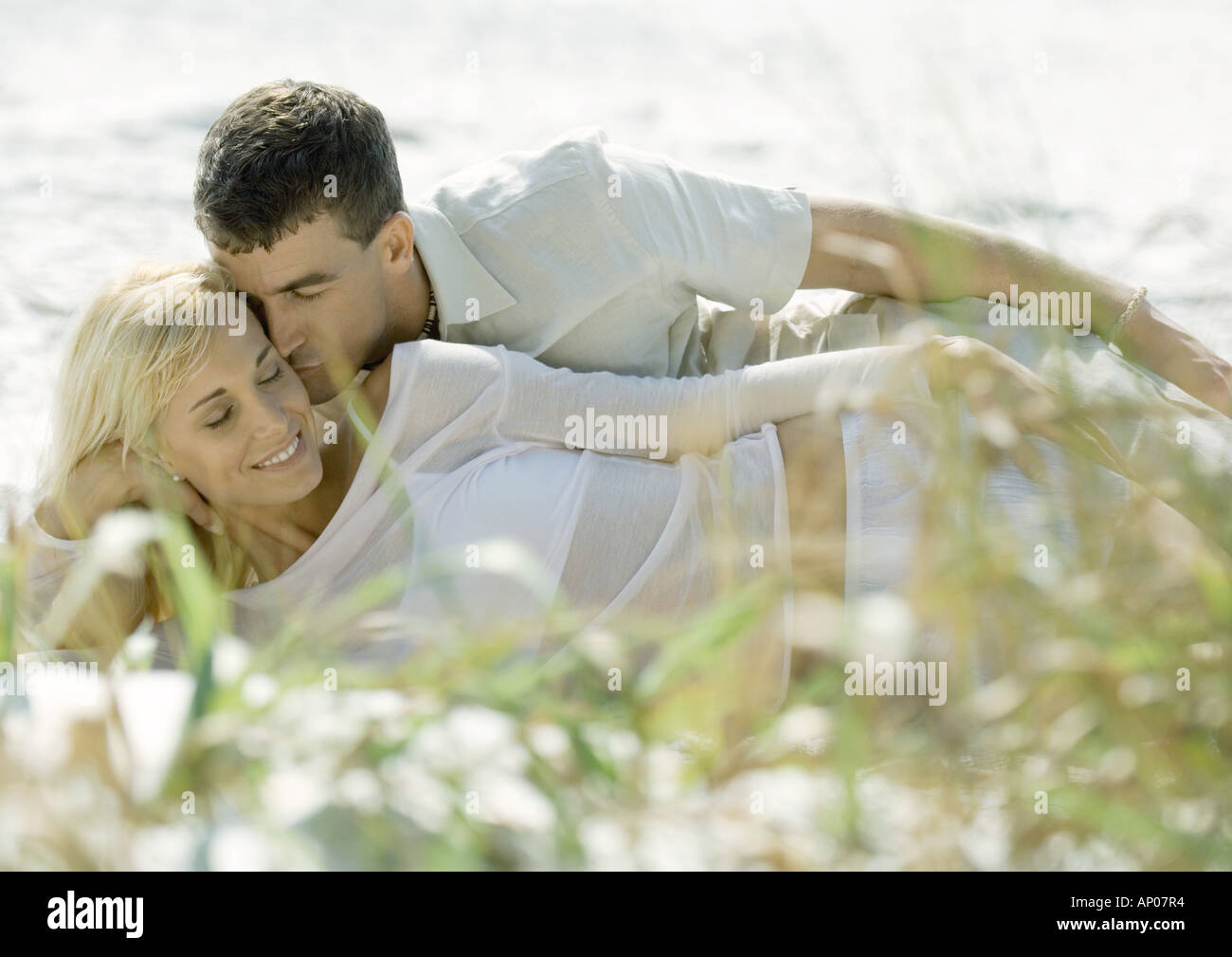Couple lying on beach, man kissing woman's cheek Stock Photo - Alamy