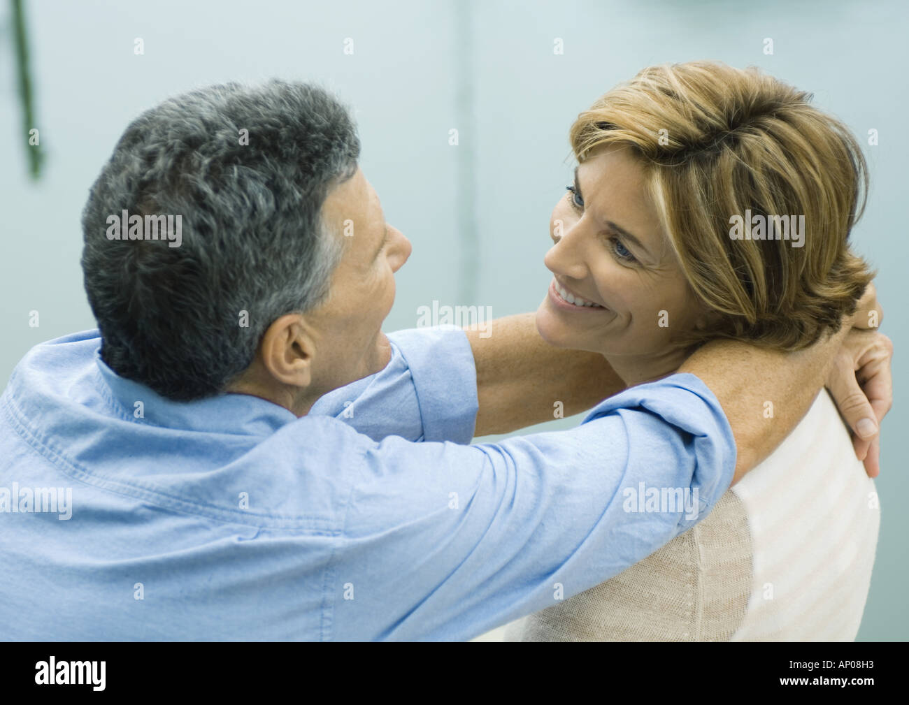 Mature couple smiling at each other, man with arms around woman's neck ...