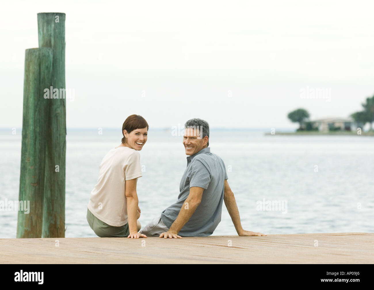 Couple sitting on edge of dock, smiling over shoulders at camera Stock ...
