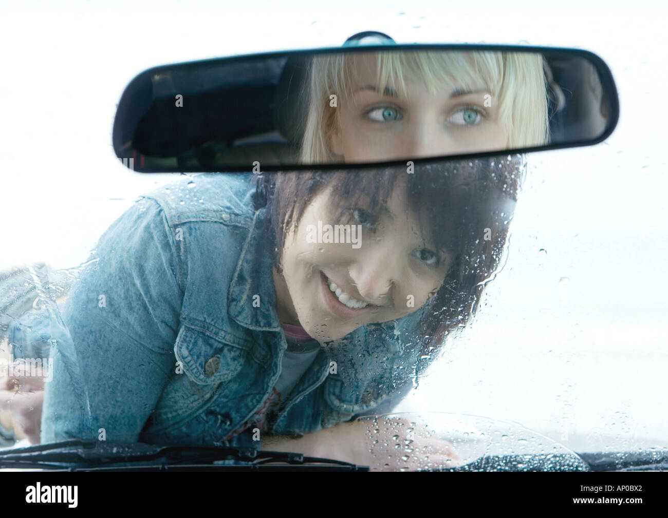 Woman lying on hood of car, looking through windshield Stock Photo - Alamy