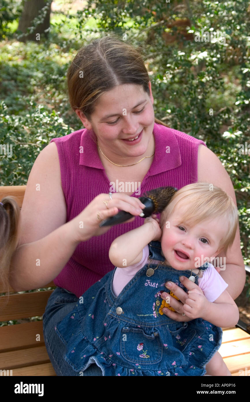 Mother brushing her baby daughter s hair as they sit on a wooden bench ...