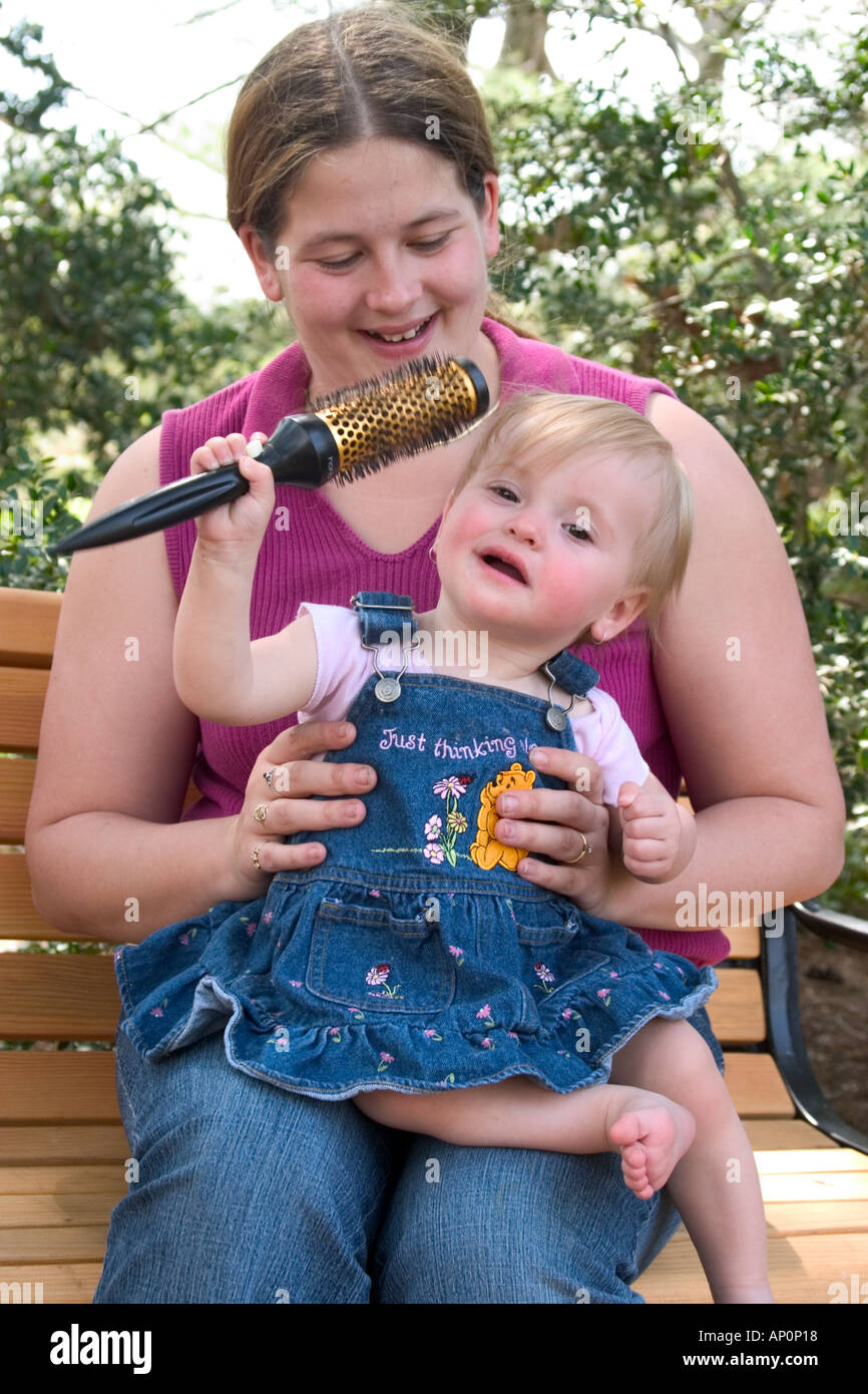 Mother brushing her baby daughter s hair as they sit on a wooden bench ...