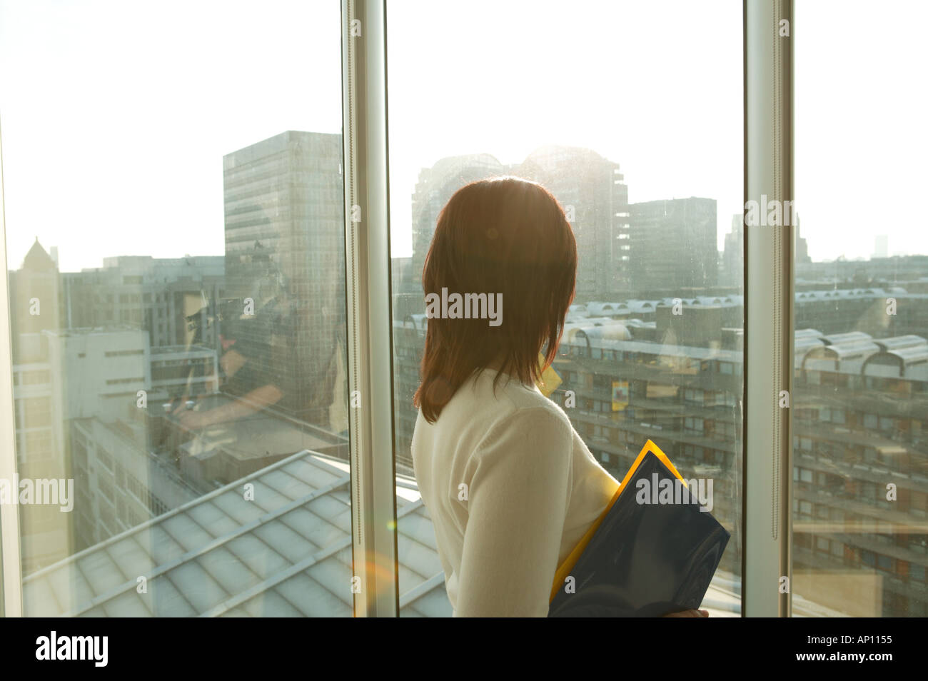 Business woman looking out of office window holding file rear view ...