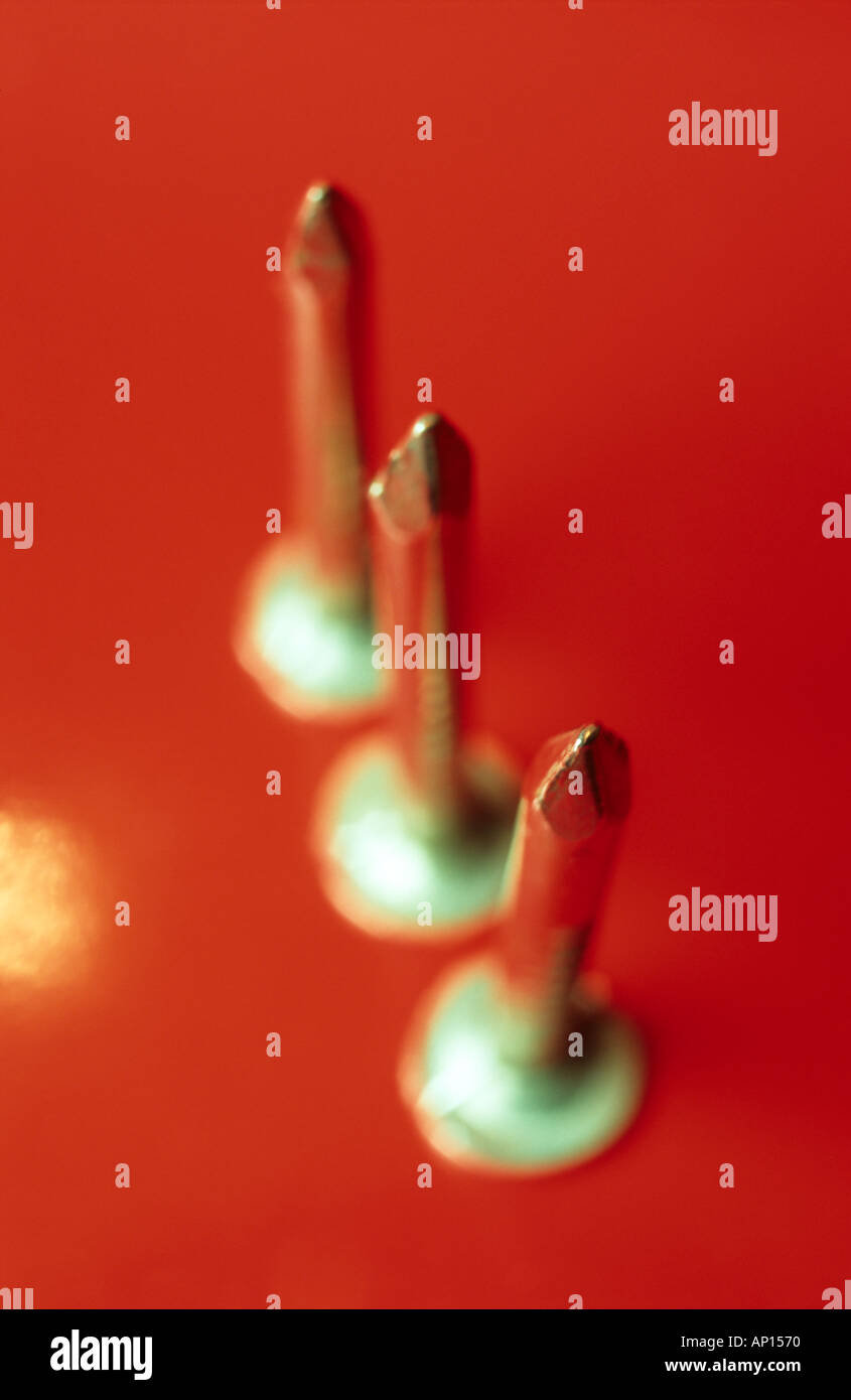 three nails in line on red background Stock Photo - Alamy