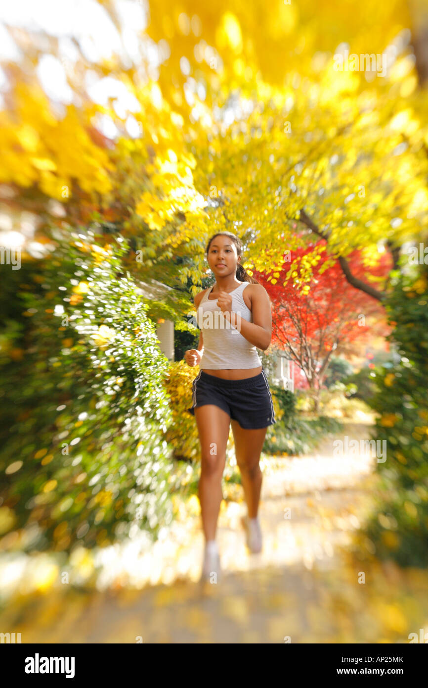 Young woman, jogging, running on a street with trees fall colors autumn ...