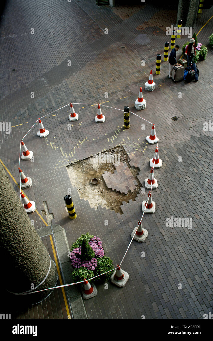 A circle of maintenance cones surrounds a hole in the pavement sidewalk ...