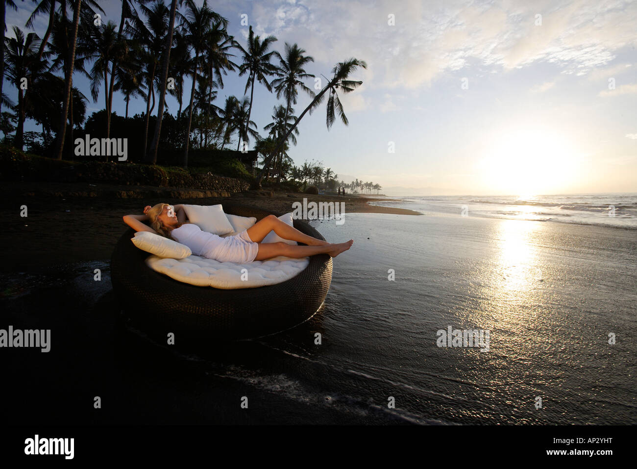 A young woman having a rest on a sun lounger on the beach at sunset ...