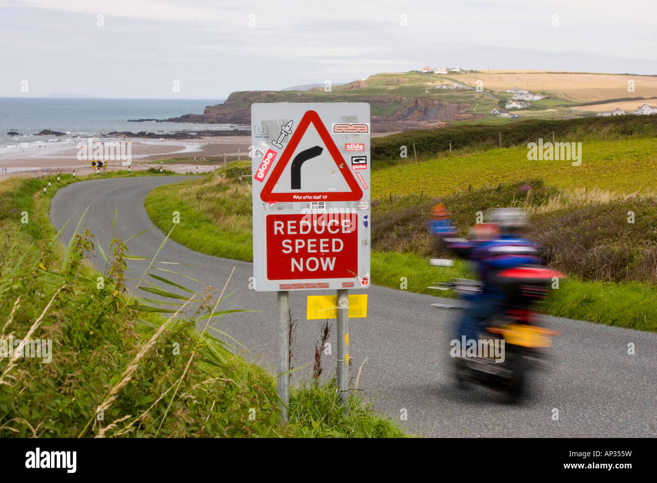 Moped passing road sign warning of dangerous bend and Reduce speed now ...