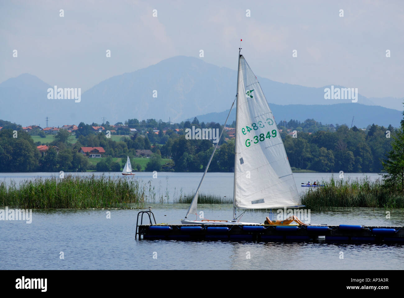 young woman sunbathing on landing stage with sailing boat, Bavarian ...
