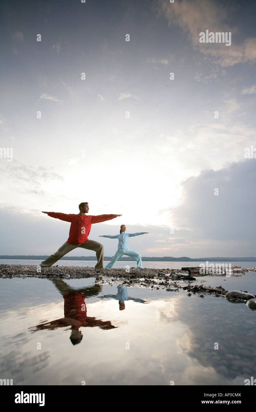 Man and woman doing yoga exercises The Warrior, reflection in the water ...