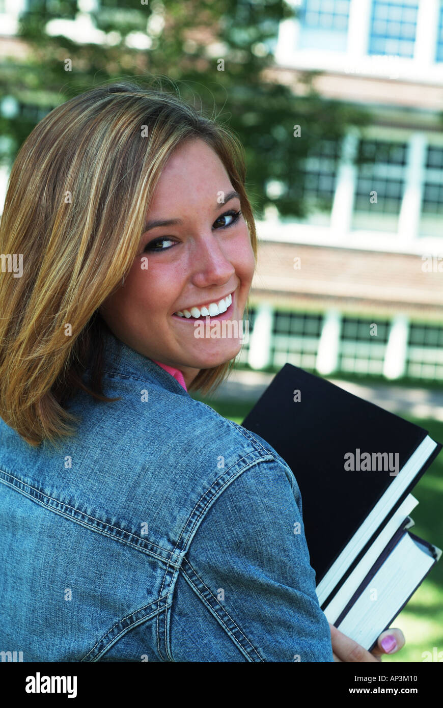 female student holding books on a school campus wearing jean jacket ...