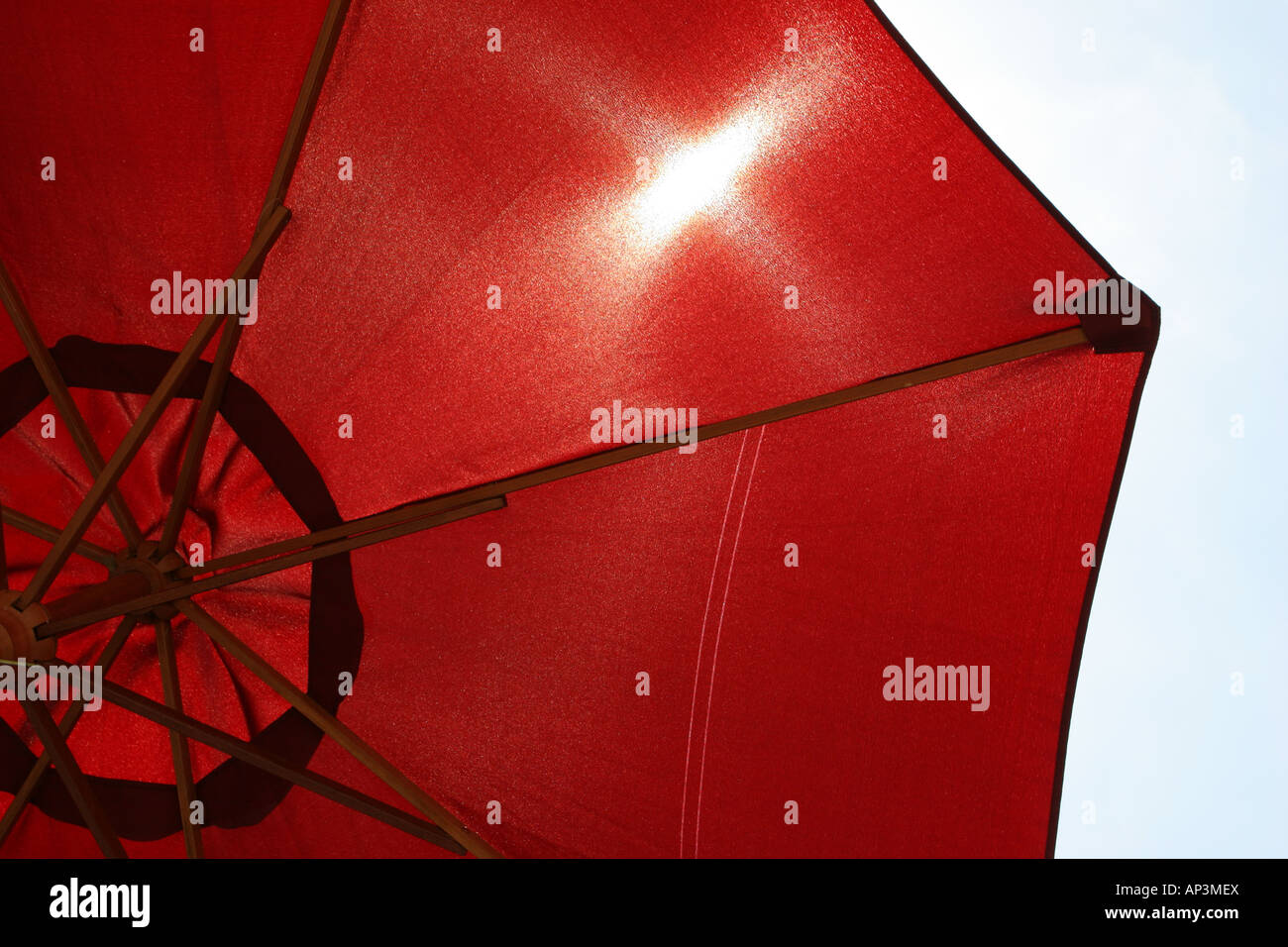 Piercing sunlight beats through the canvass material of a red parasol ...