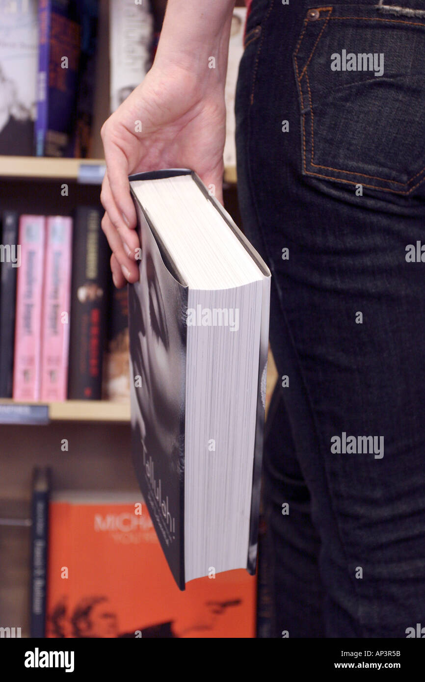 A close up of a hardback book in a womans hand, in front of a bookshelf ...
