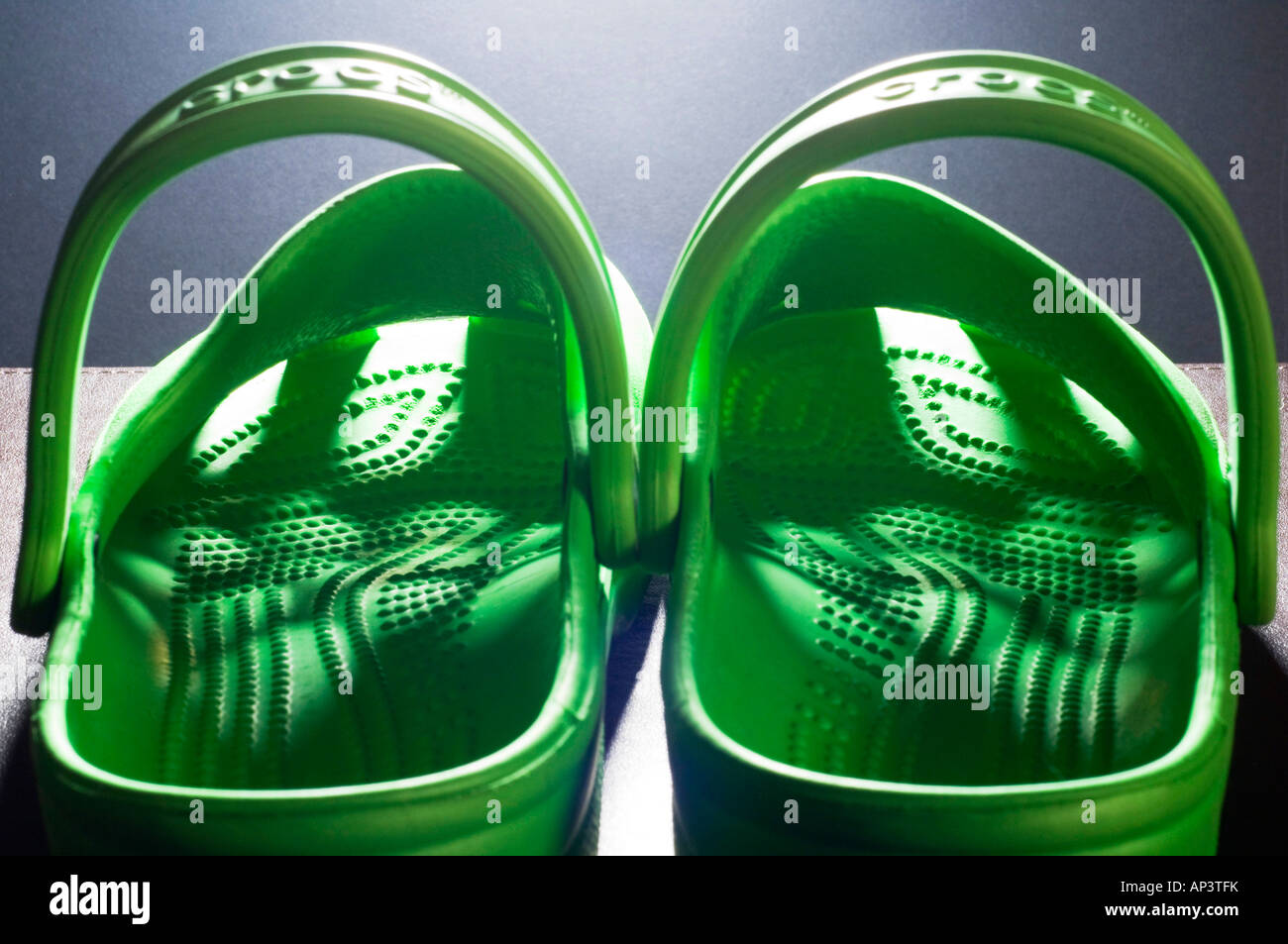 A pair of bright green Crocs clogs with light shining through the ...