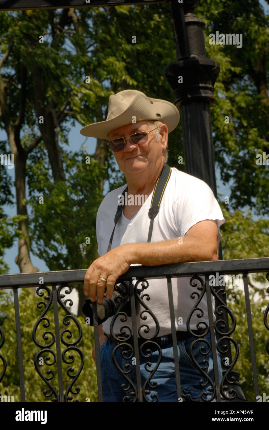 Man with cowboy had leaning against railing with camera Stock Photo - Alamy