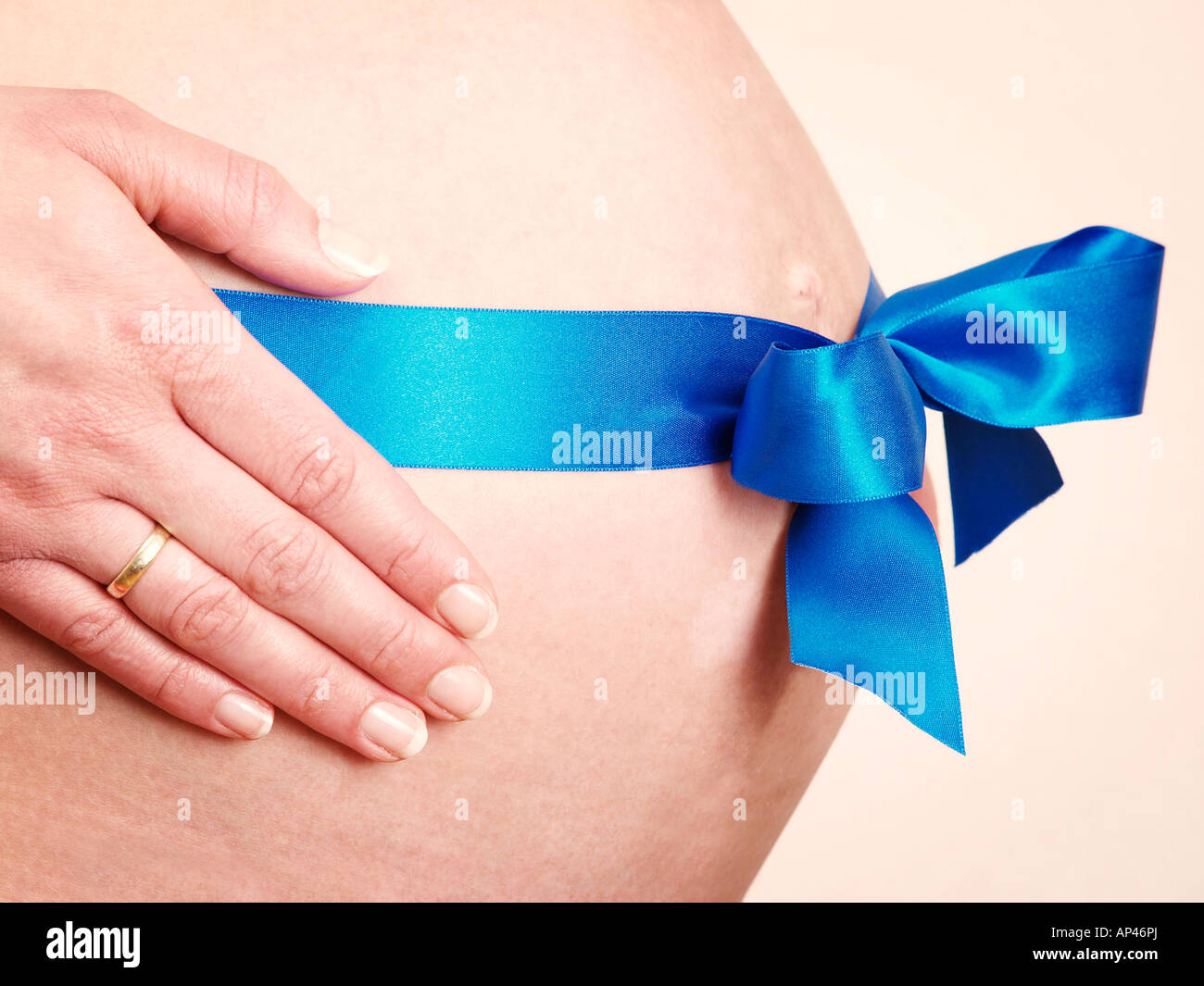 Belly of pregnant woman with big blue ribbon and hand Stock Photo - Alamy