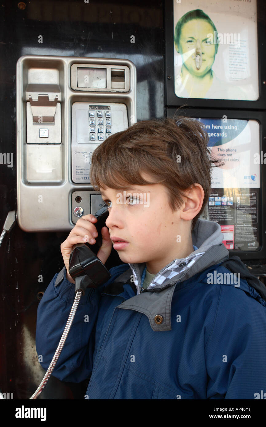 Young boy aged 11 years using a public telephone in a callbox to ring ...