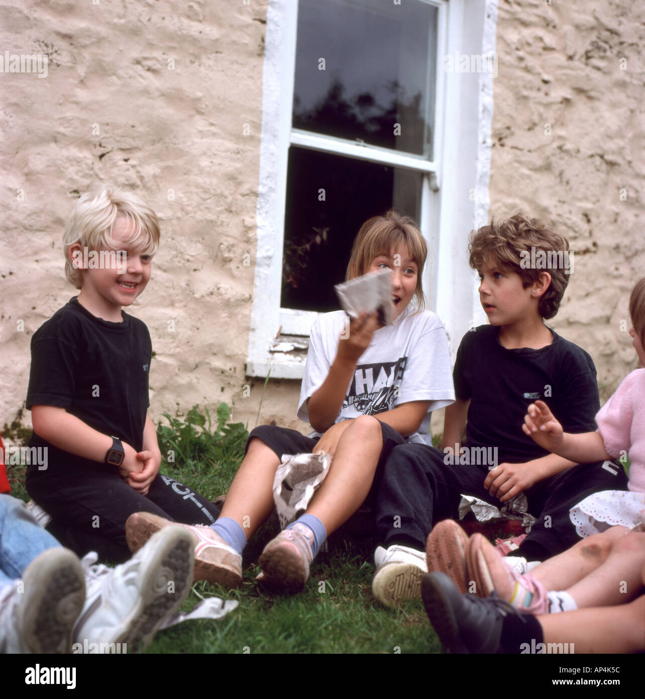 British children sitting outside in the garden in playing a pass the ...