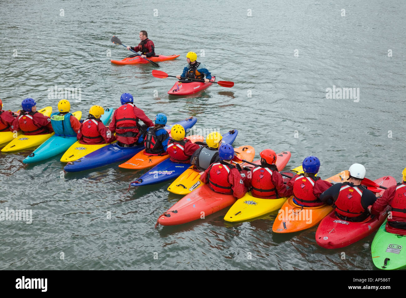 Colourful kayaks lined up on water for canoeing lesson with instructor ...