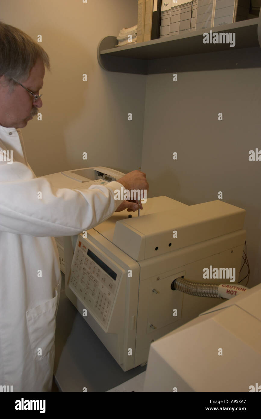 Toxicologist using a gas chromatograph to test a sample for traces of ...