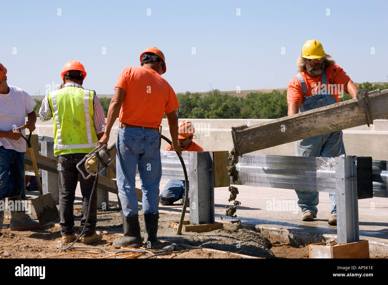 Highway construction crew installing a guardrail and laying concrete on ...