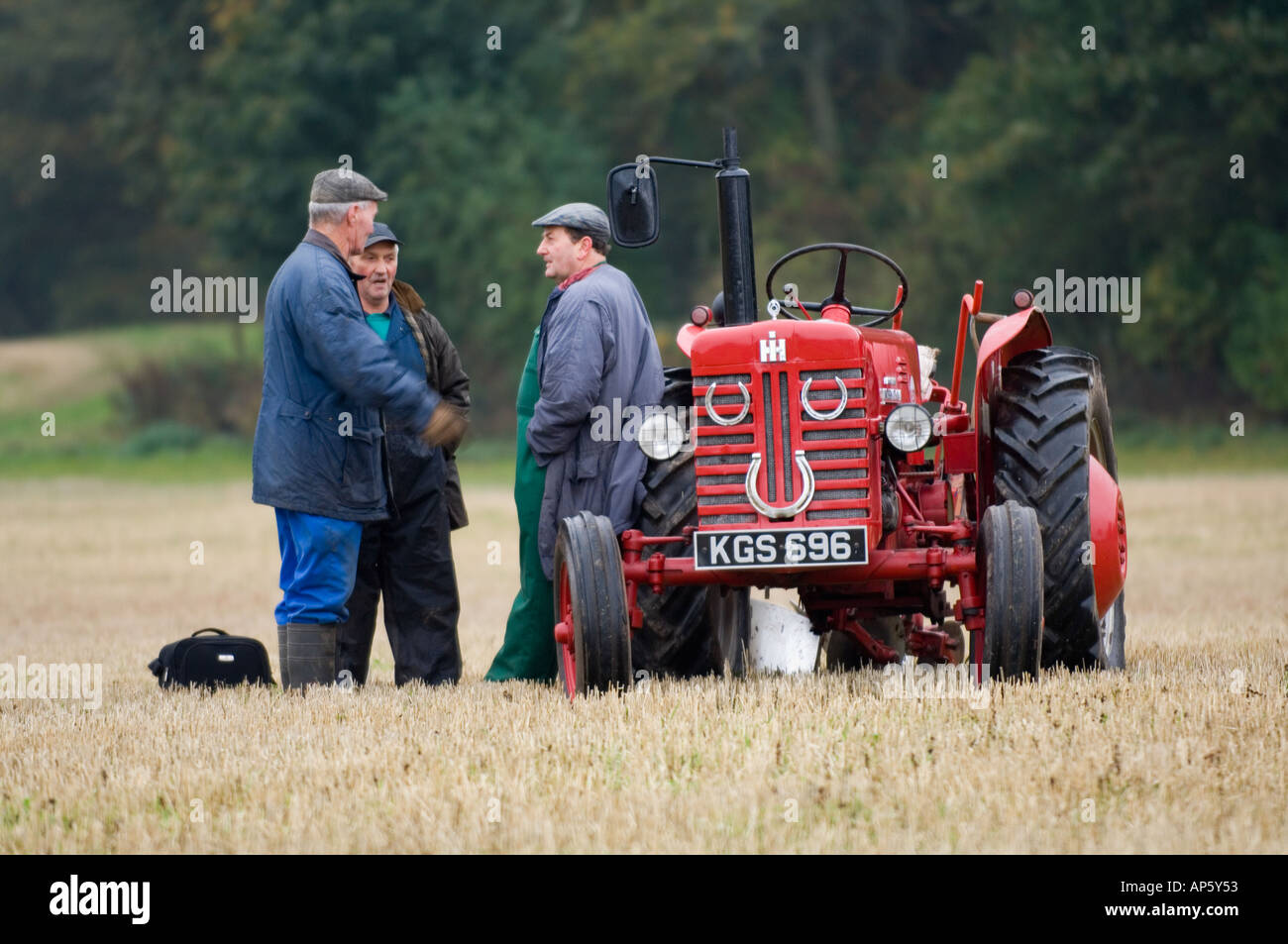 Three farmers talking near a red tractor Stock Photo - Alamy