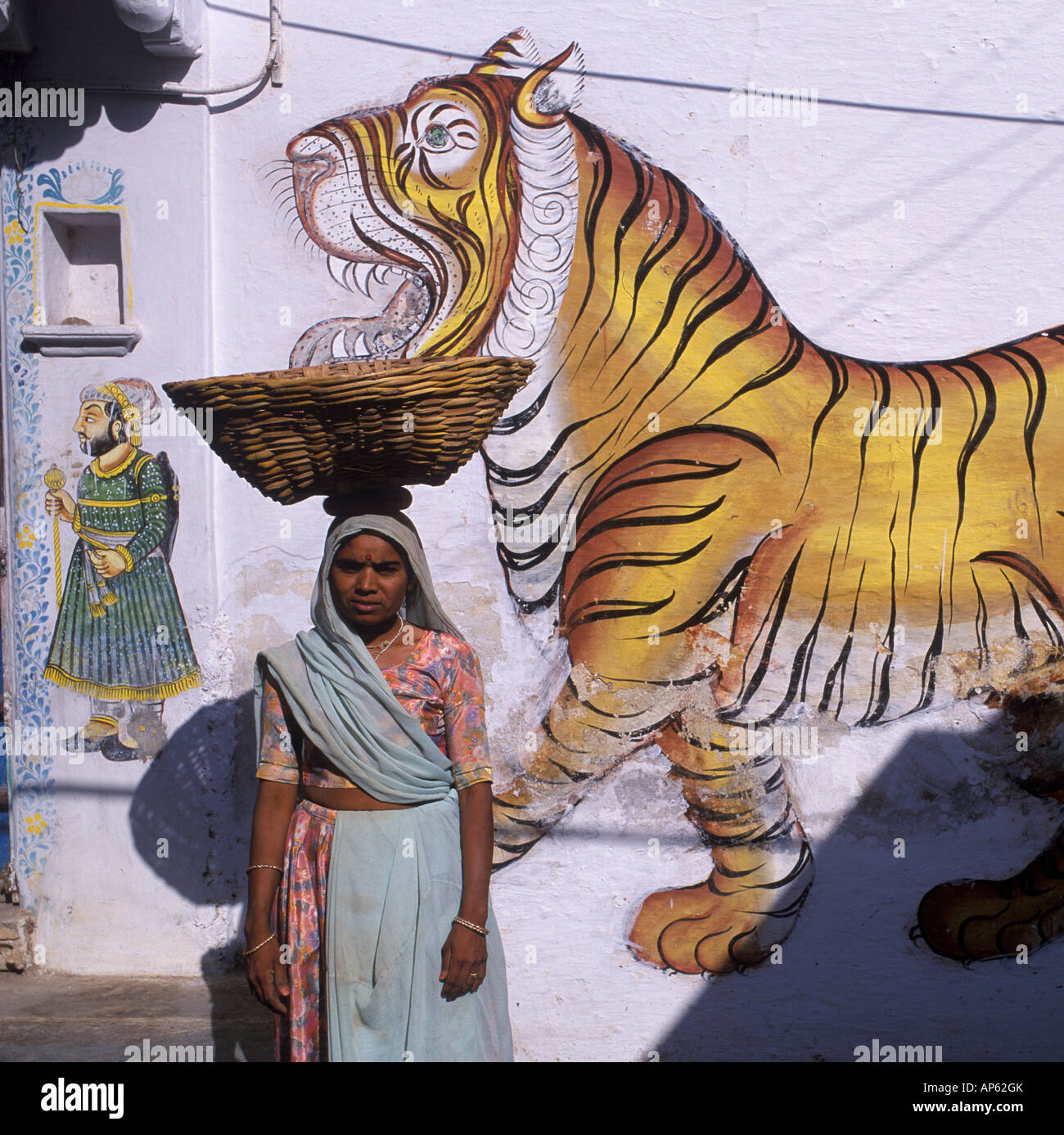 Woman with basket on head in front of Rajput tiger on wall, Udaipur ...