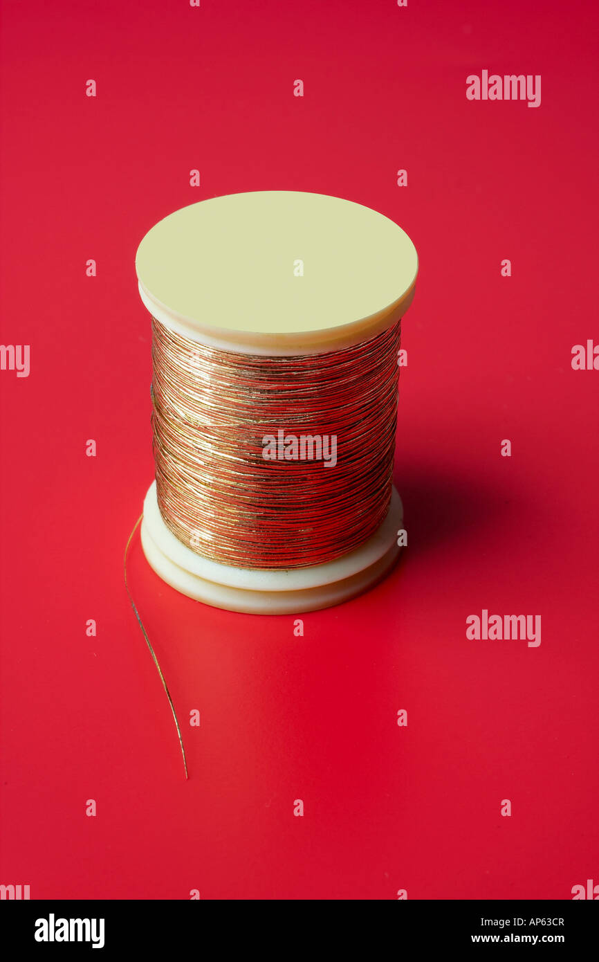 bobbin of golden thread on a red background Stock Photo - Alamy