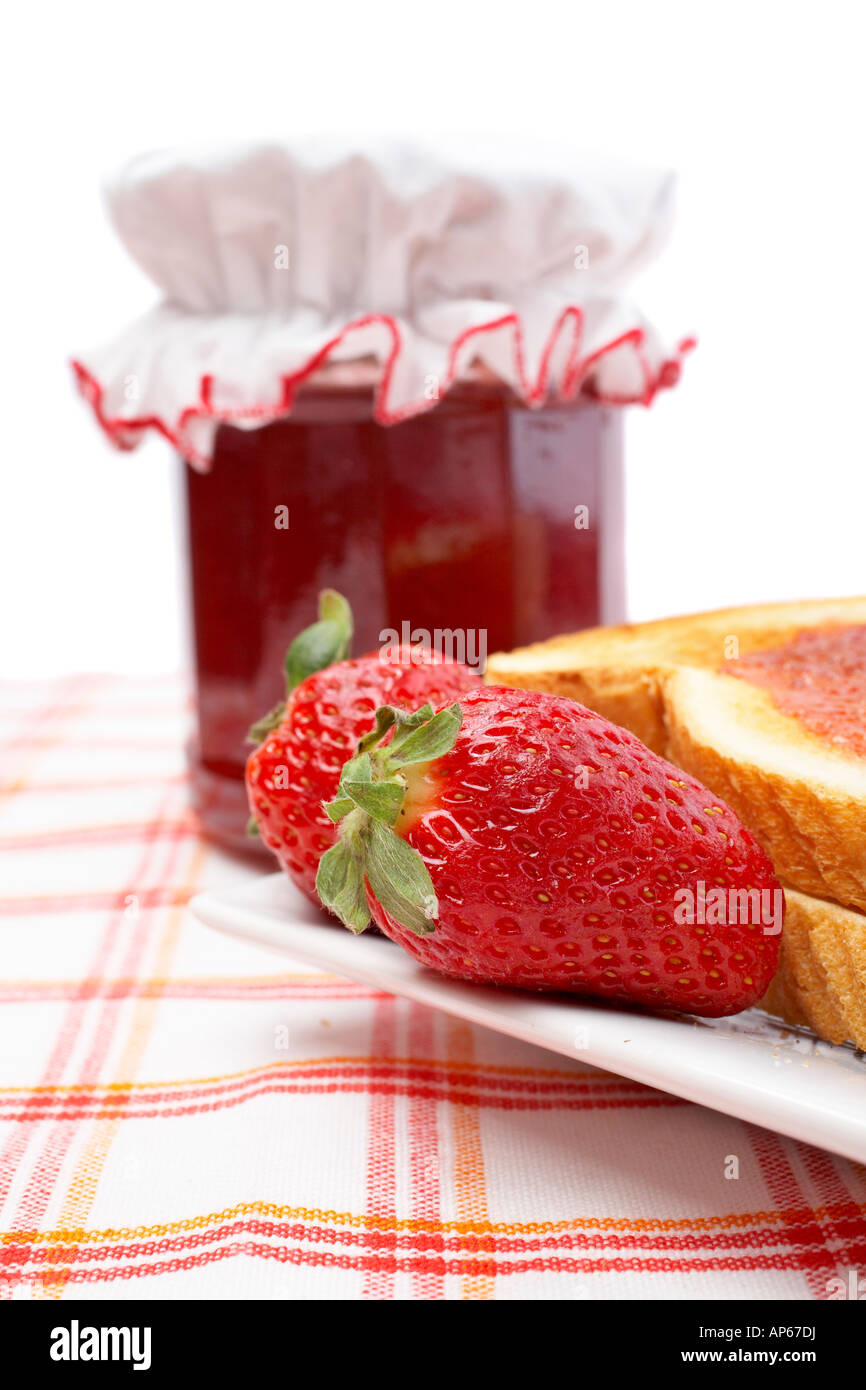 Two strawberries and toasts in a dish in front of jam jar Shallow DOF ...