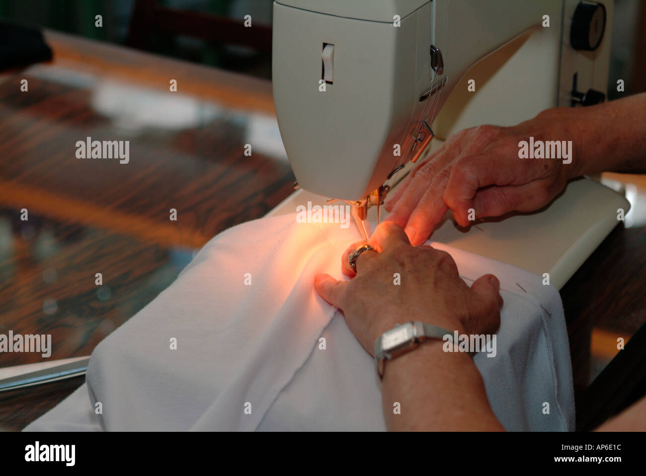 Close up of a woman using a domestic sewing machine to sew white cotton ...