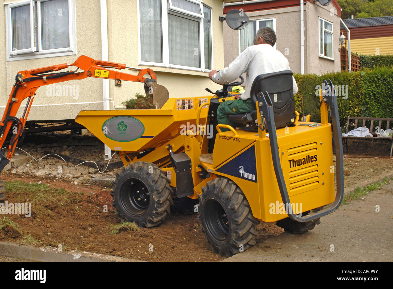 A mini digger dumping soil into a mini dumper truck Stock Photo - Alamy