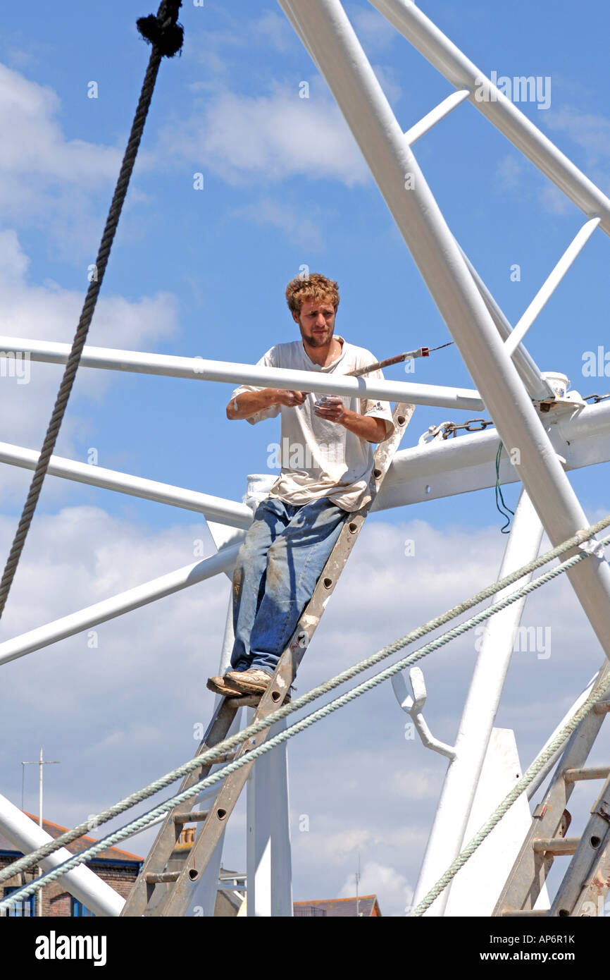 Fishing boat crew member using a long handled paint roller during a ...