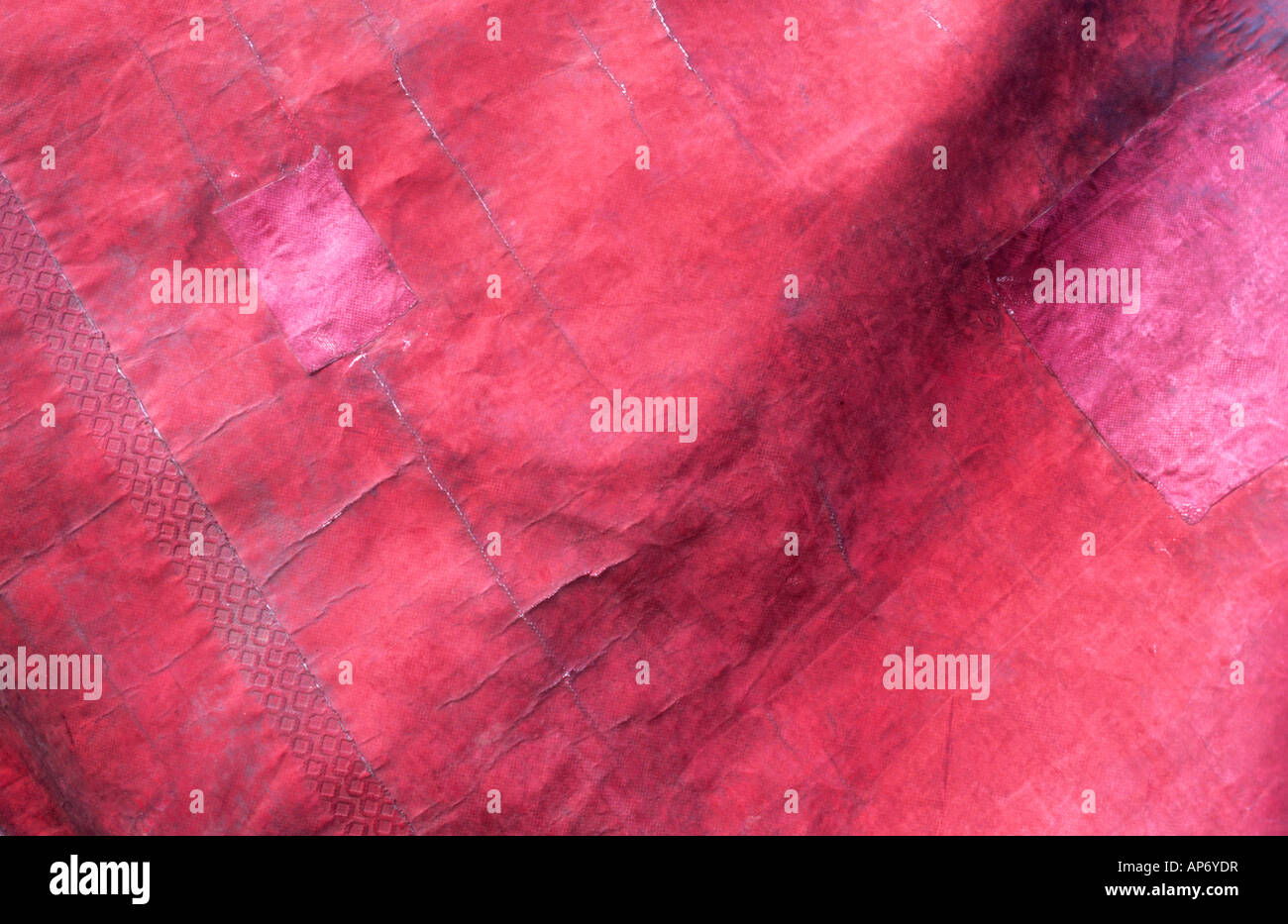 Detail of dirty red plastic or nylon tarpaulin sheet with paler red ...
