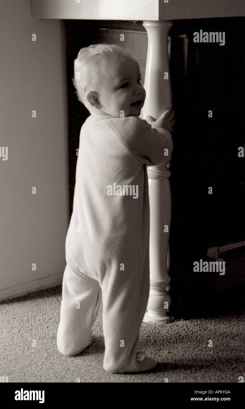 vertical monochrome of baby standing for the first time whilst holding ...