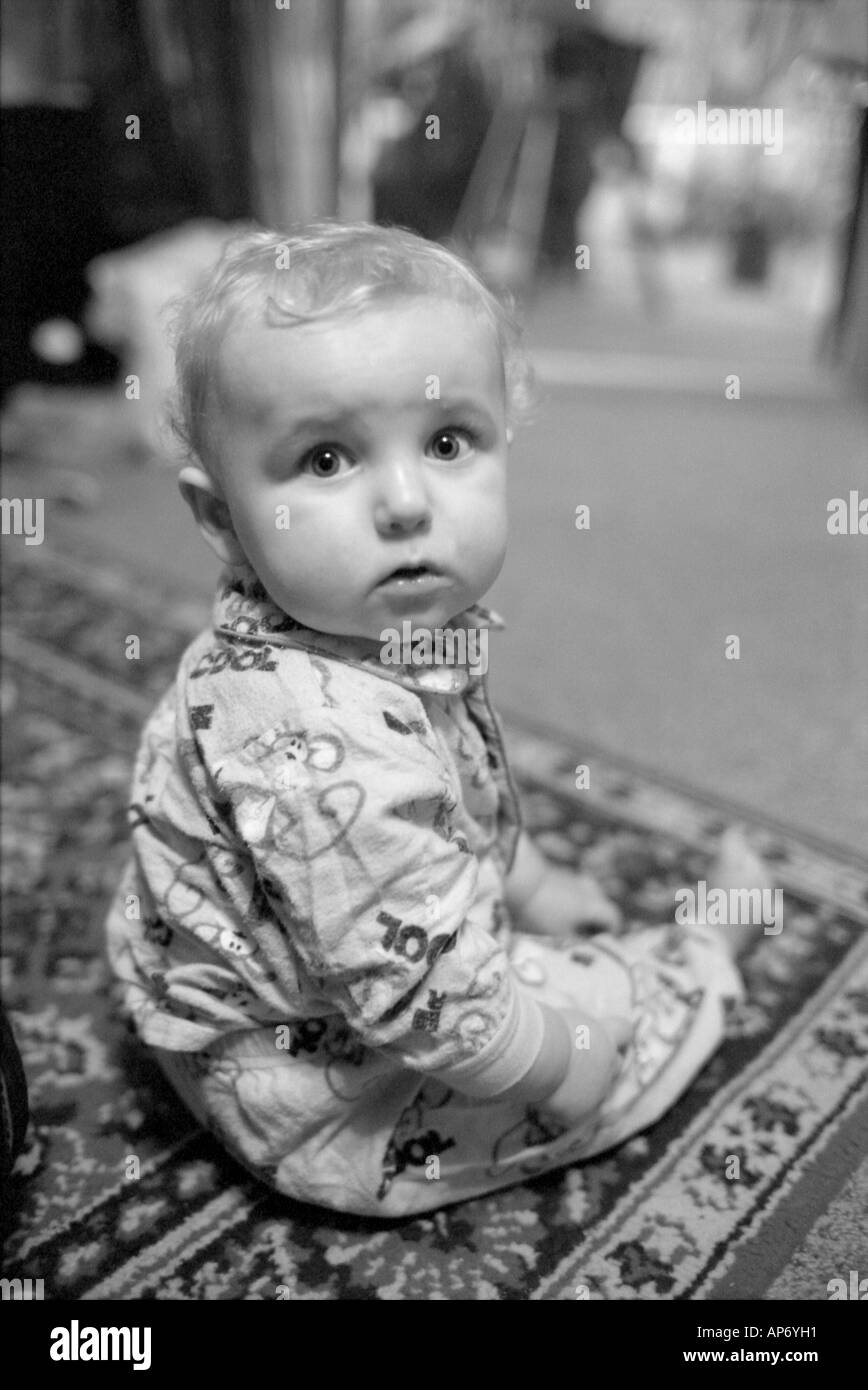 monochrome of baby looking over shoulder at the camera whilst sitting ...