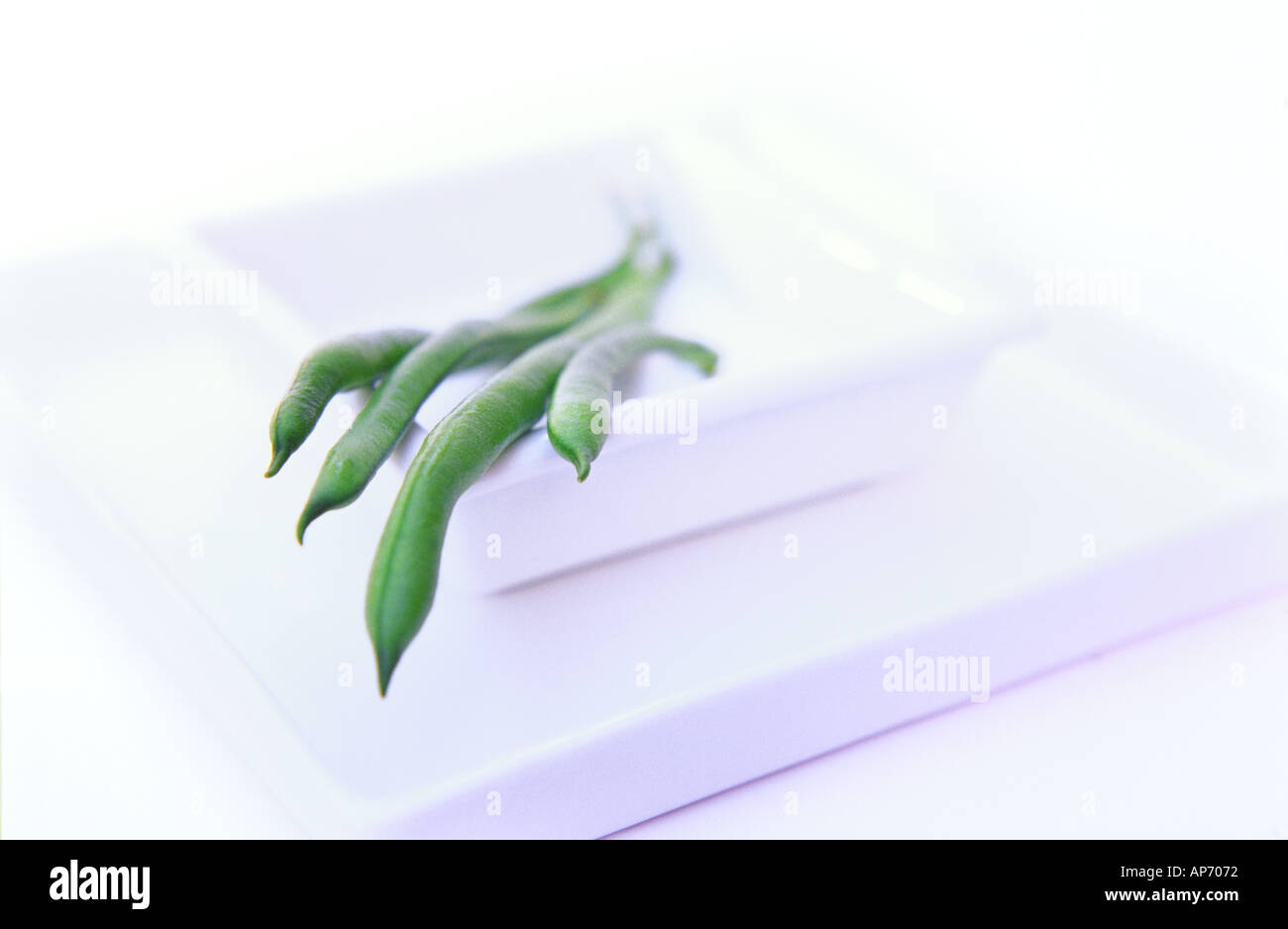 Green fresh string beans tantalisingly hanging over a set of square ...