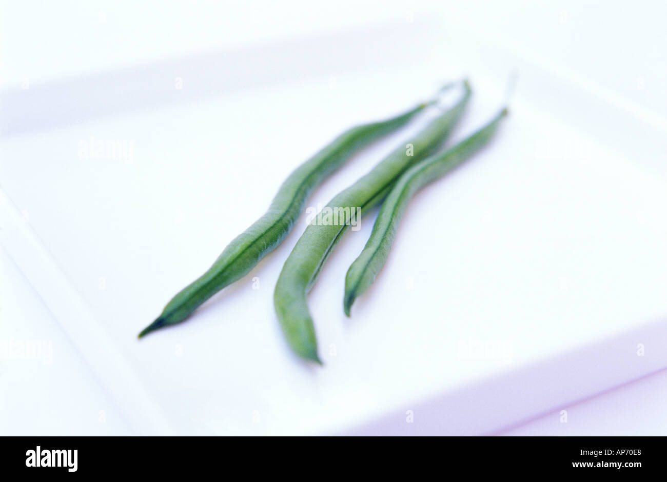 Three strands of green fresh string beans arranged on a white square ...