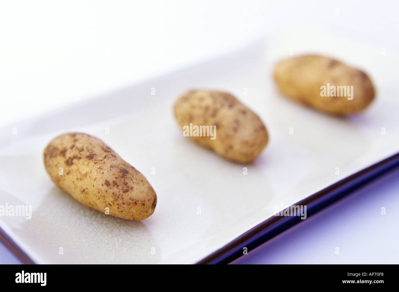 Three young potatoes on a rectangular plate against a white background ...