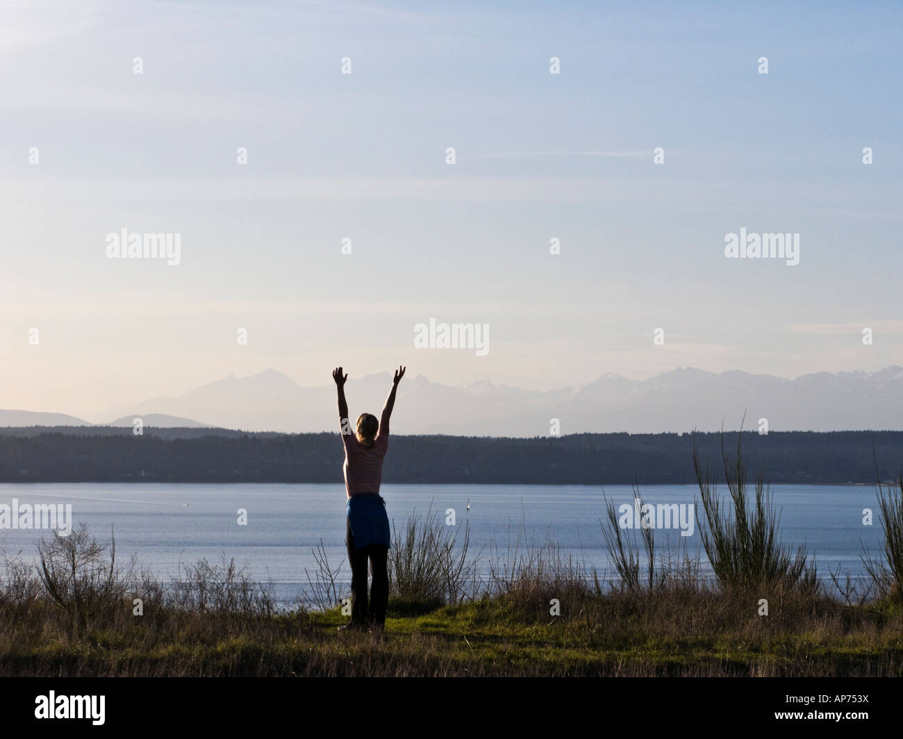 Woman with arms above head outstretched toward sky and mountains ...